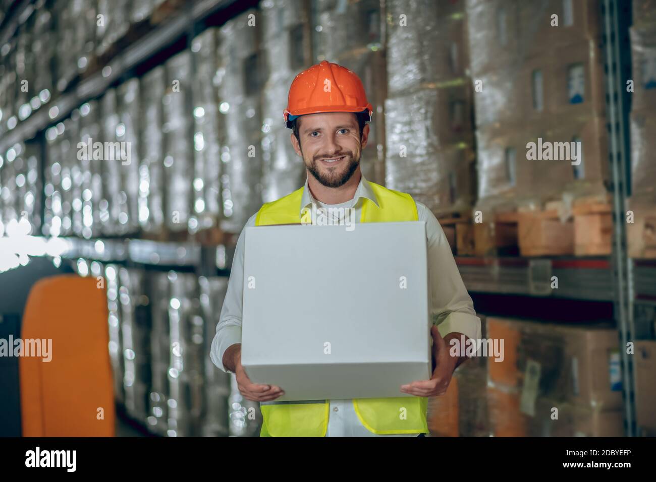 Young male bearded worker carrying a box and smiling Stock Photo - Alamy