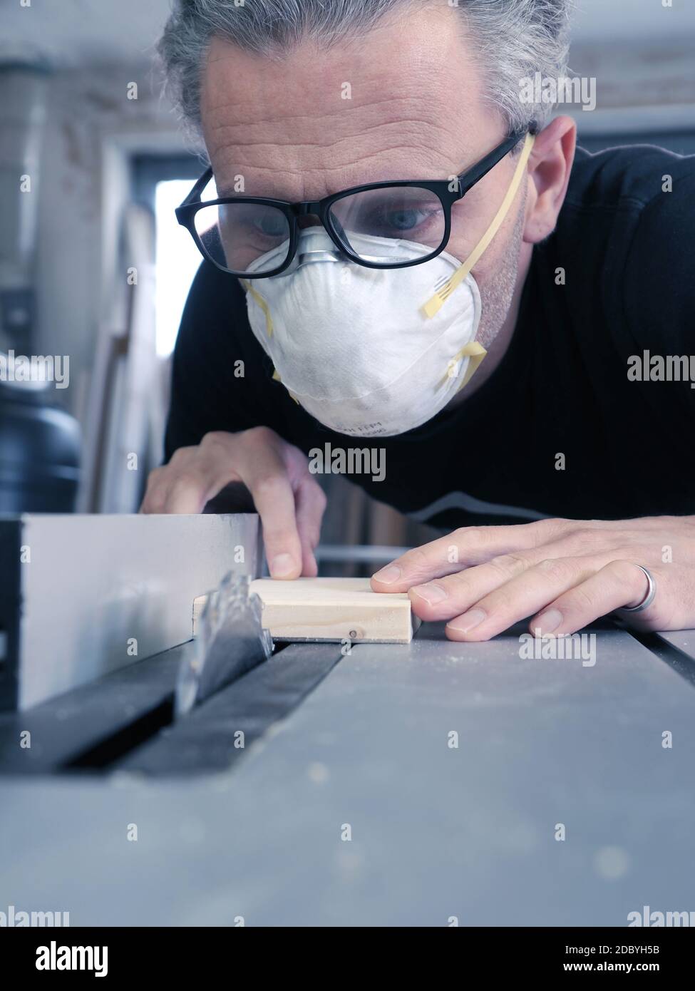 Man with a dust mask and goggles working on a circular saw ...