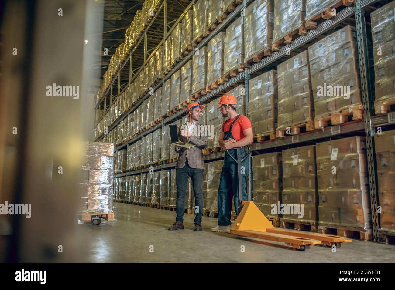 Two men in orange helmets talking in the warehouse Stock Photo - Alamy