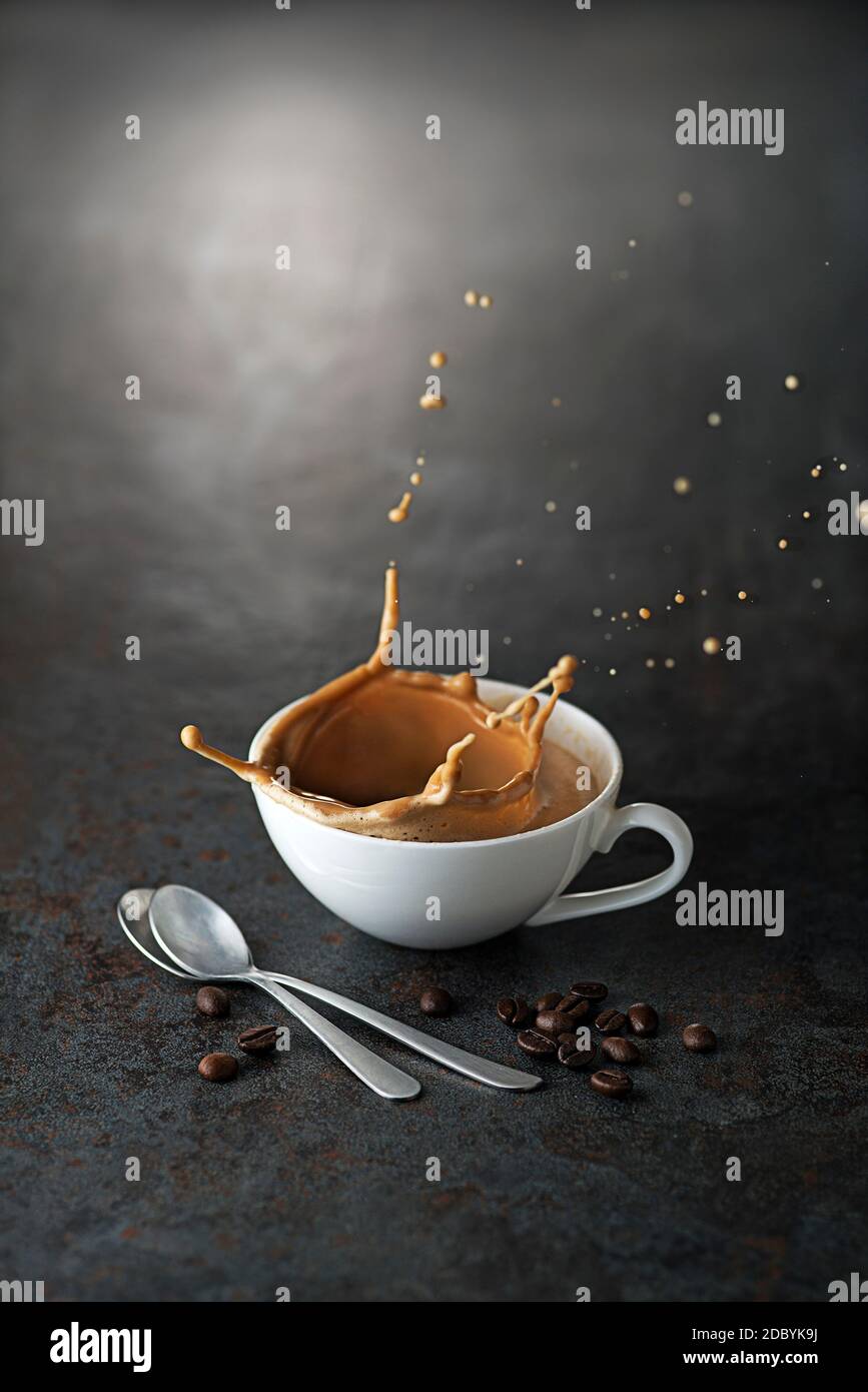 Porcelain white cup with splashing coffee liquid on dark background ...