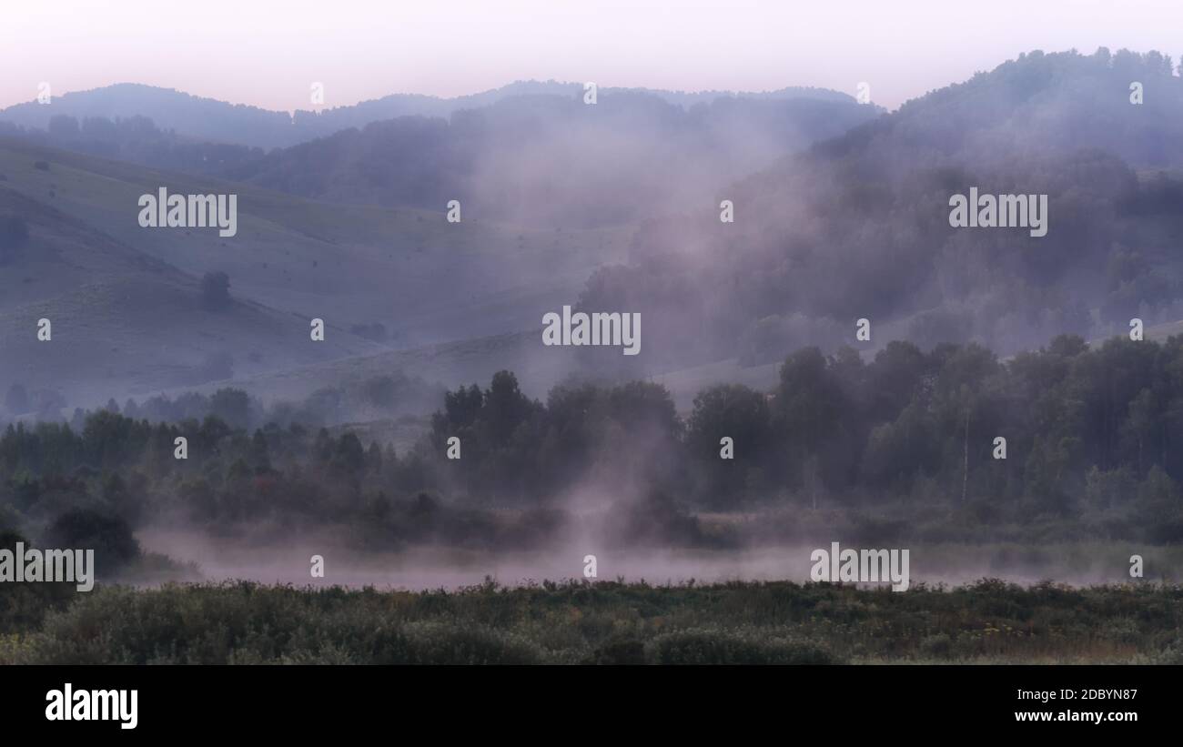 landscape in the early morning with fog over the water, mountains in ...