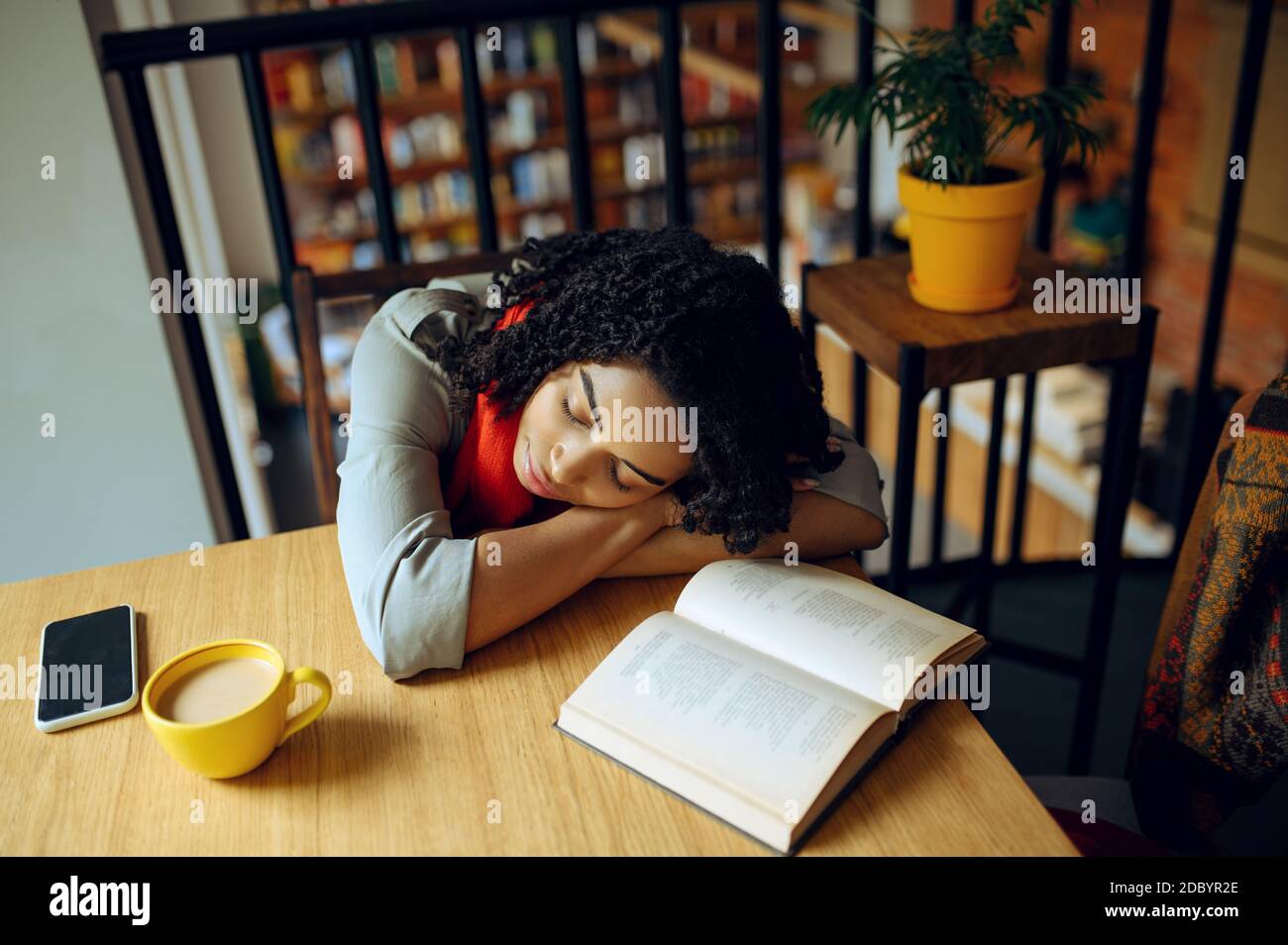 Tired female student sleeps at the table in cafe. Woman learning a ...