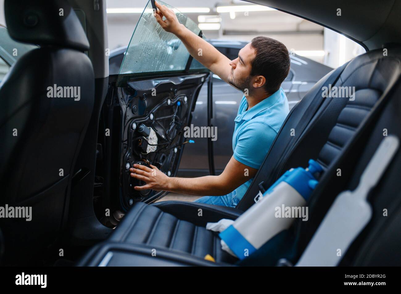 Male worker prepares car for tinting, tuning service. Mechanic applying ...