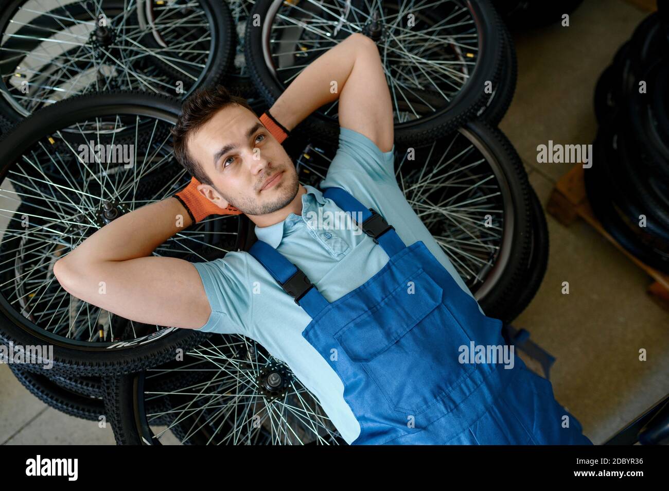Male worker lying on stack of bicycle wheels on factory. Bike rims ...