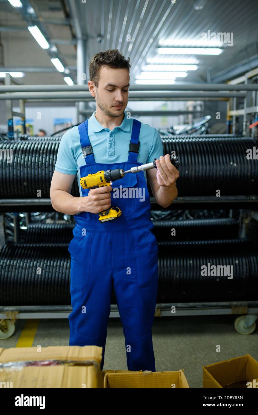Worker in uniform holds electric screwdriver and bicycle hub, rows of ...