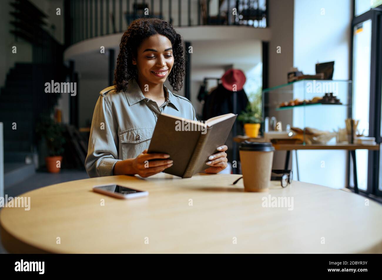 Smiling female student reads a book in cafe. Woman learning a subject ...
