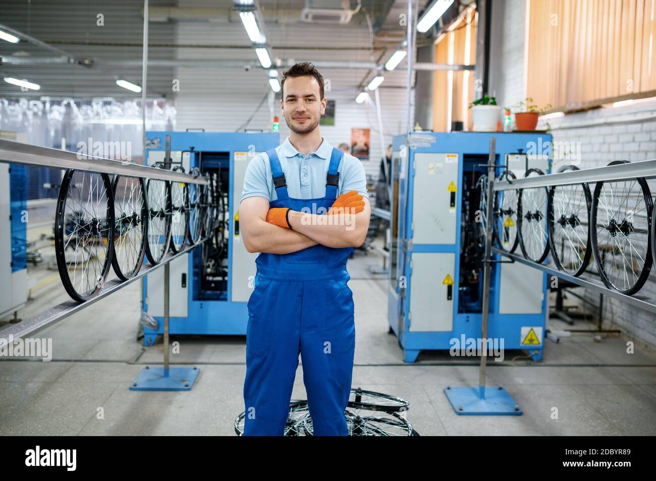 Worker in uniform poses on bicycle wheel factory. Bike rims and spokes ...
