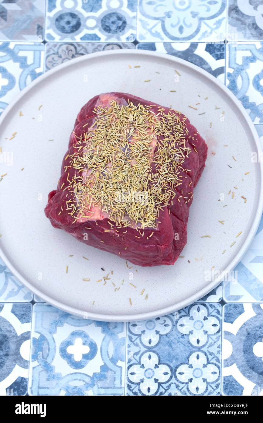 Raw beef roasting joint covered with rosemary on a grey plate. Blue ...