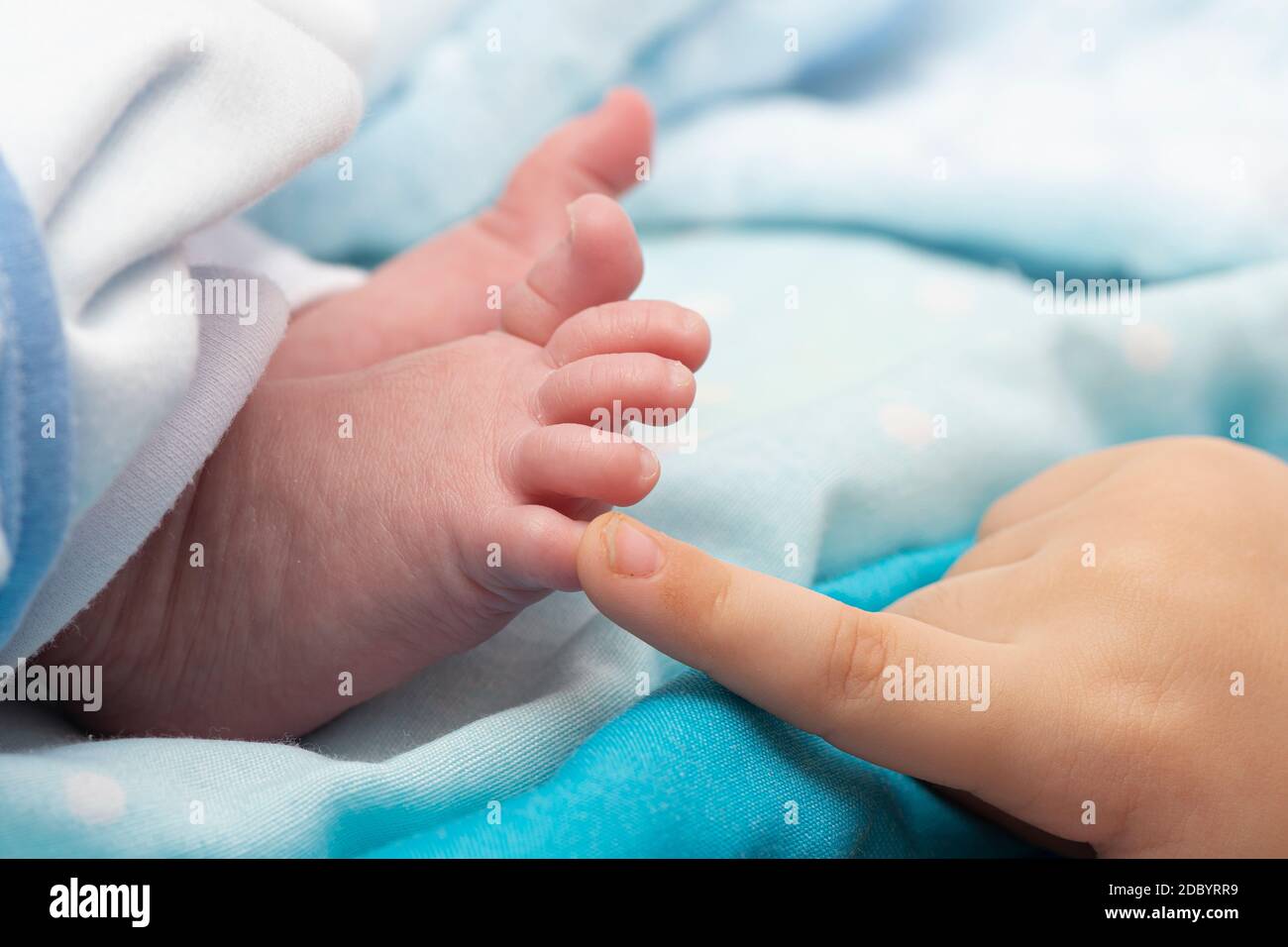 A little girl touching newborn baby foot at bed- close-up macro shot ...