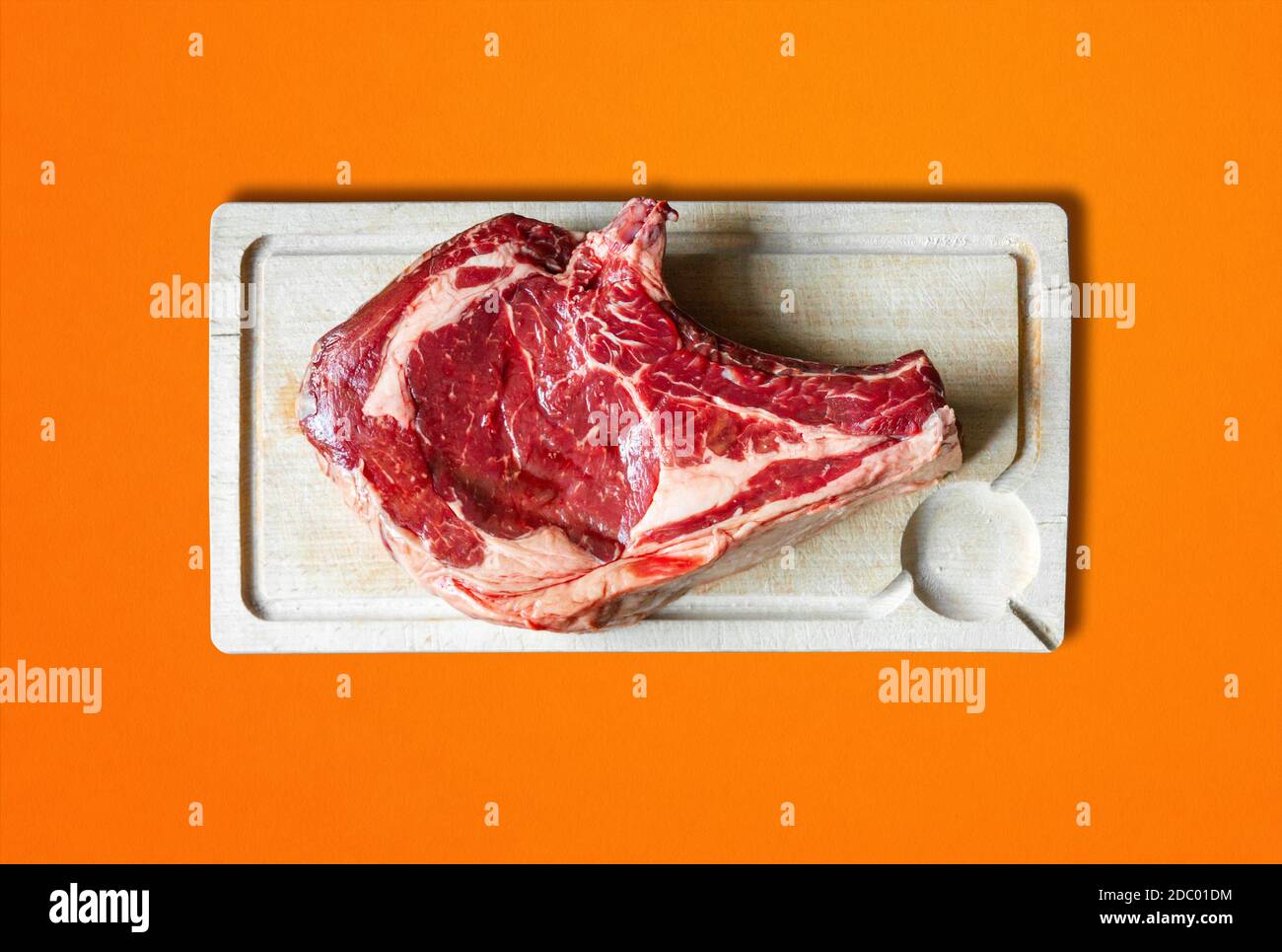 Raw beef prime rib on a cutting board. Orange background. Top view ...