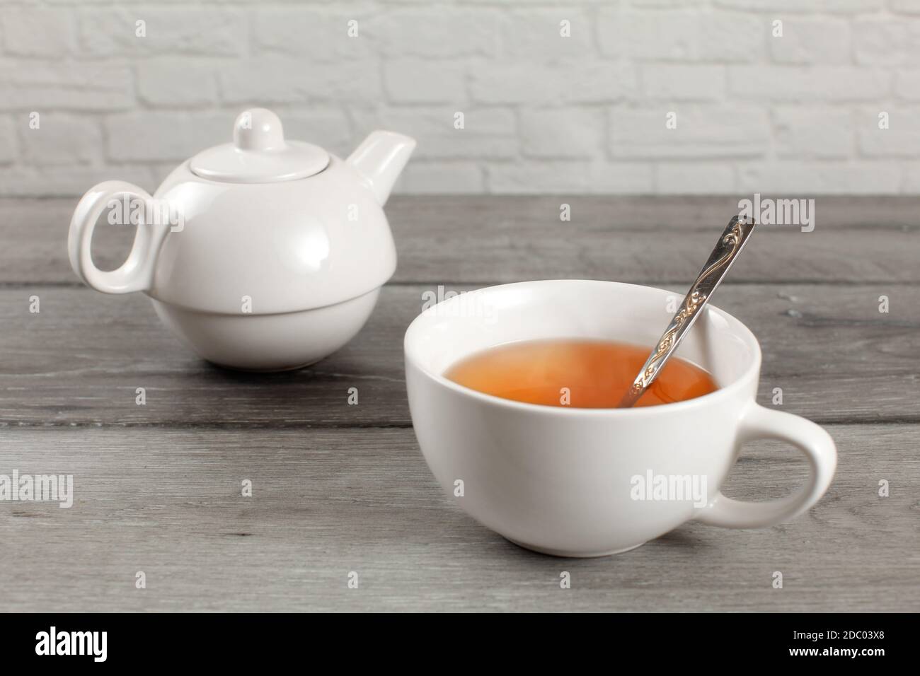 White ceramic teapot and cup of hot amber tea on gray wood desk Stock ...