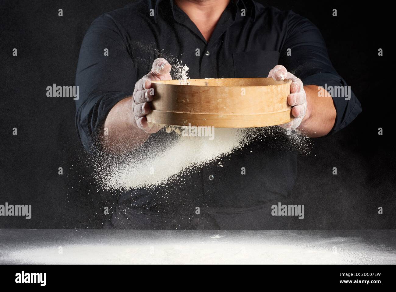 man in a black uniform holds a round wooden sieve in his hands and ...