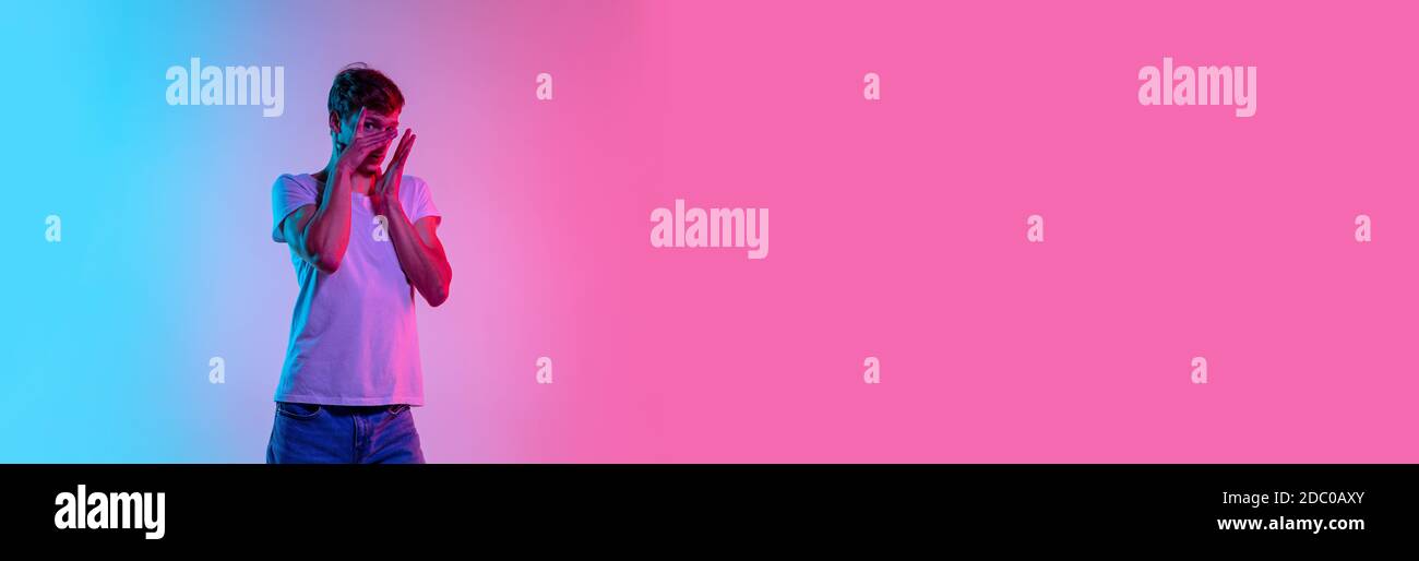 Scared, flyer. Young caucasian man's portrait on gradient blue-pink ...