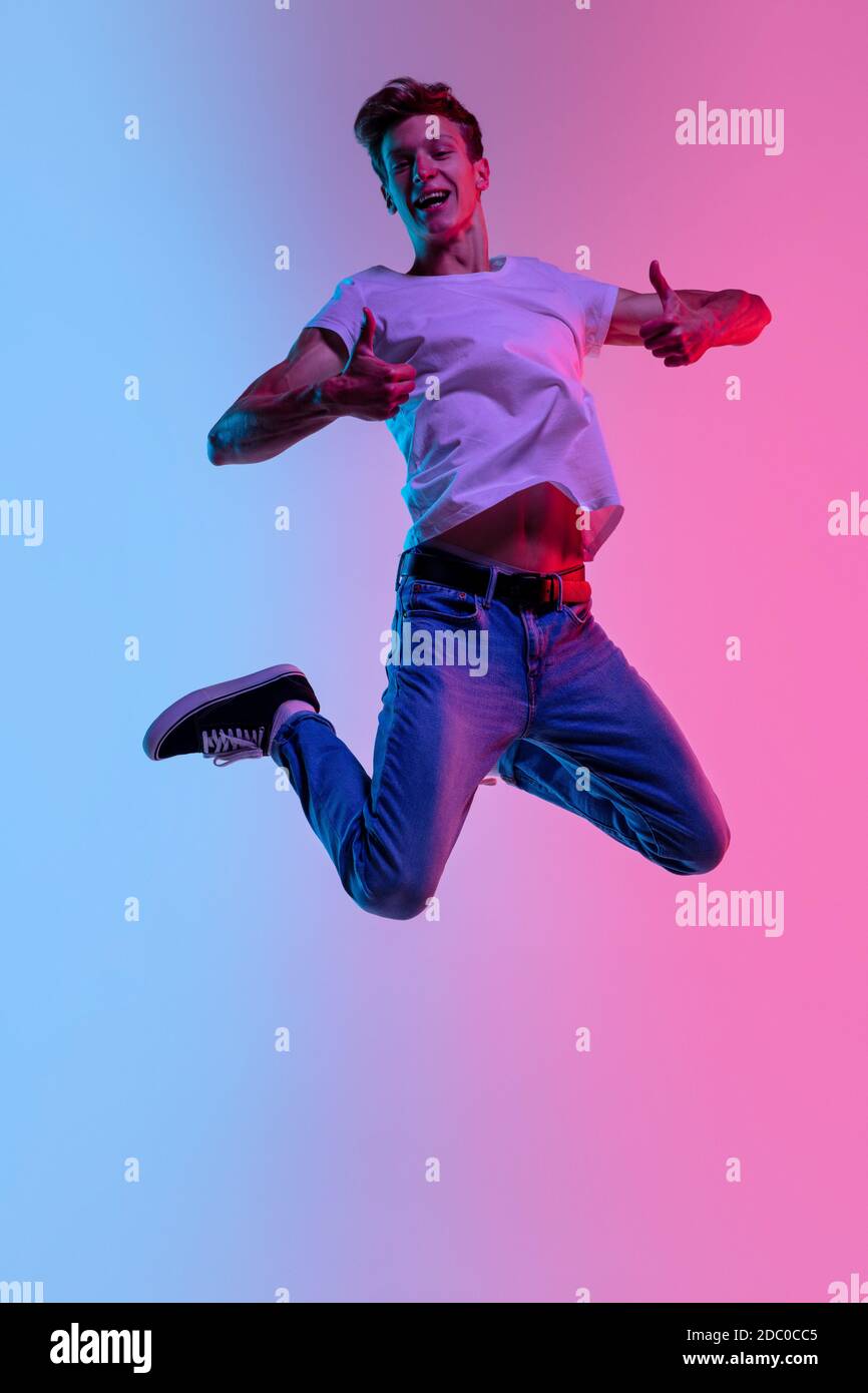 Thumbs up. Young caucasian man's jumping high on gradient blue-pink ...