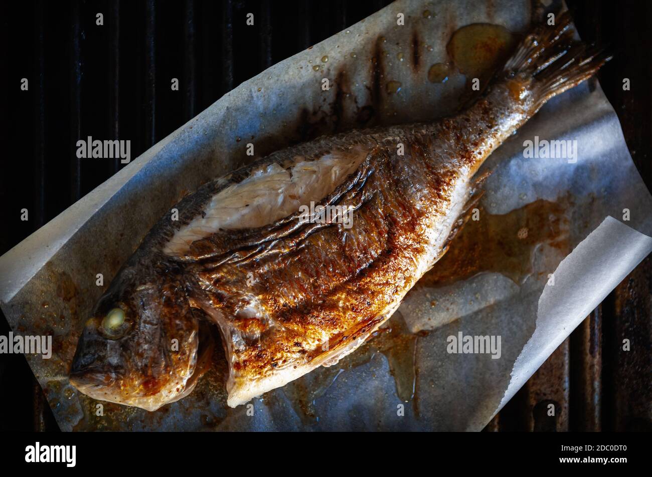 Whole dorada fish cooking in seafood restaurant kitchen on grill pan ...