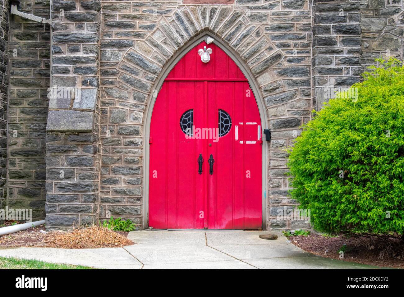 A Bright Red Door in a Cobblestone Church Wall With a Bush on the Side ...