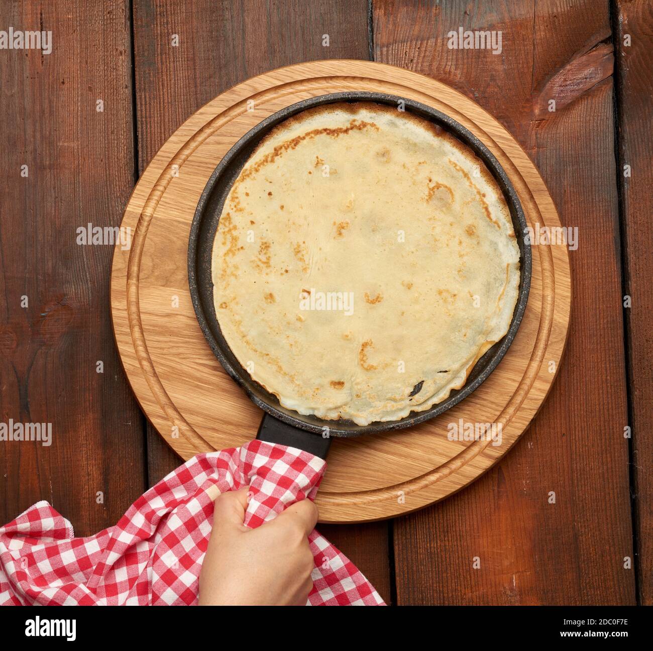 baked round big pancake in a black frying pan on a brown wooden table ...
