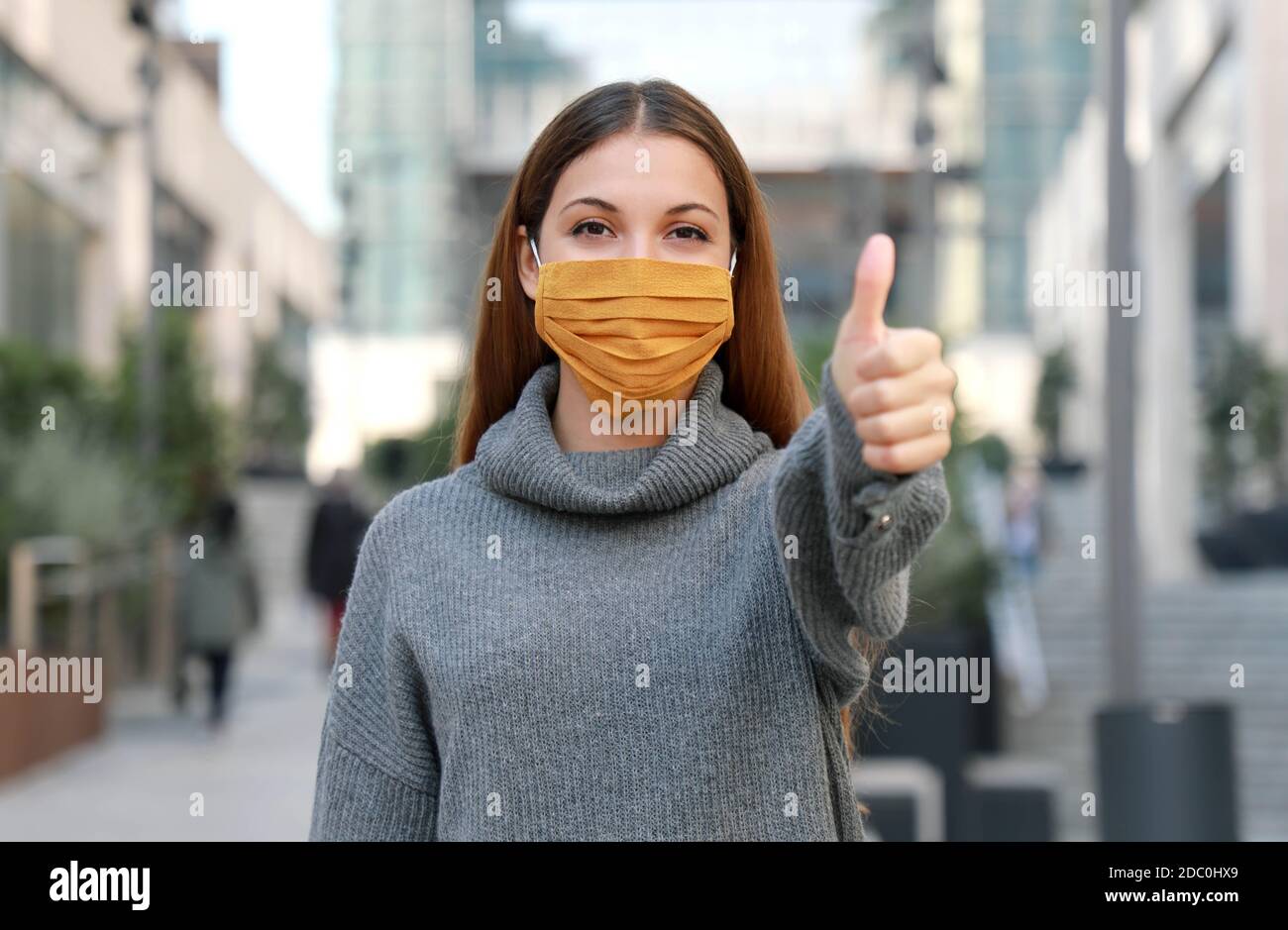 Use the mask! Young woman wearing protective face mask showing thumbs ...