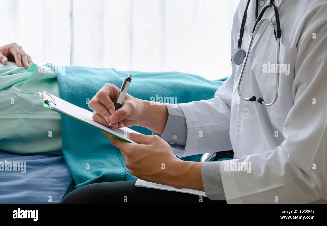 Close up of doctor writing on a medical chart with patient lying on ...