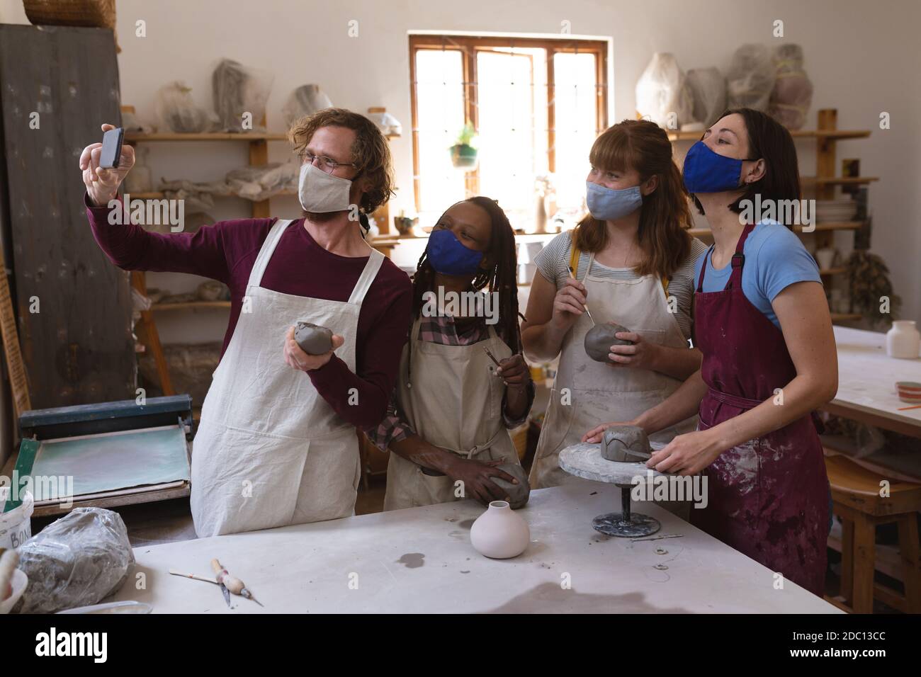 Multi-ethnic group of potters in face masks working in pottery studio ...