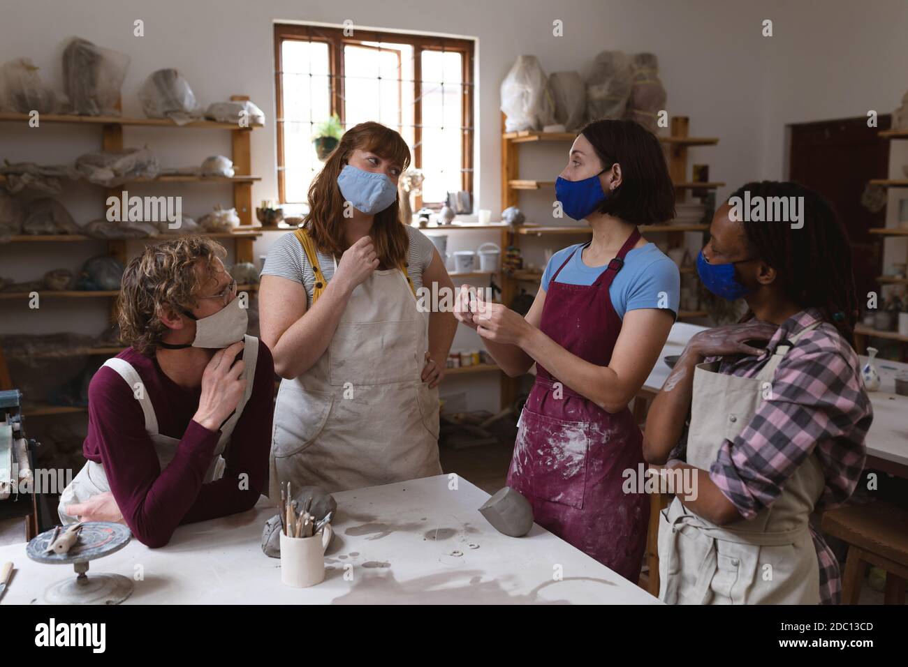 Multi-ethnic group of potters in face masks working in pottery studio ...