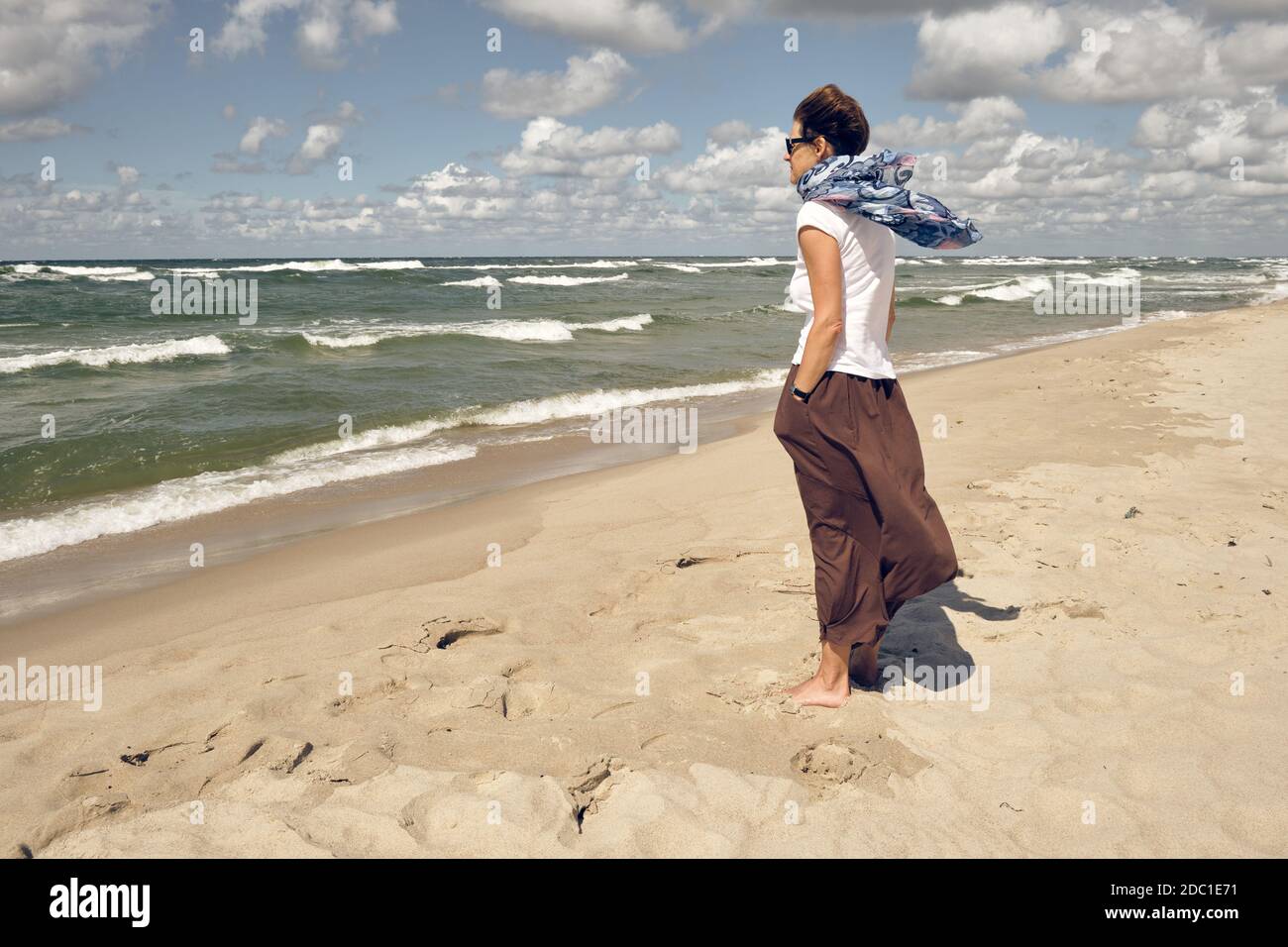 Lonely middle aged woman on the beach looking at sea on windy summer ...
