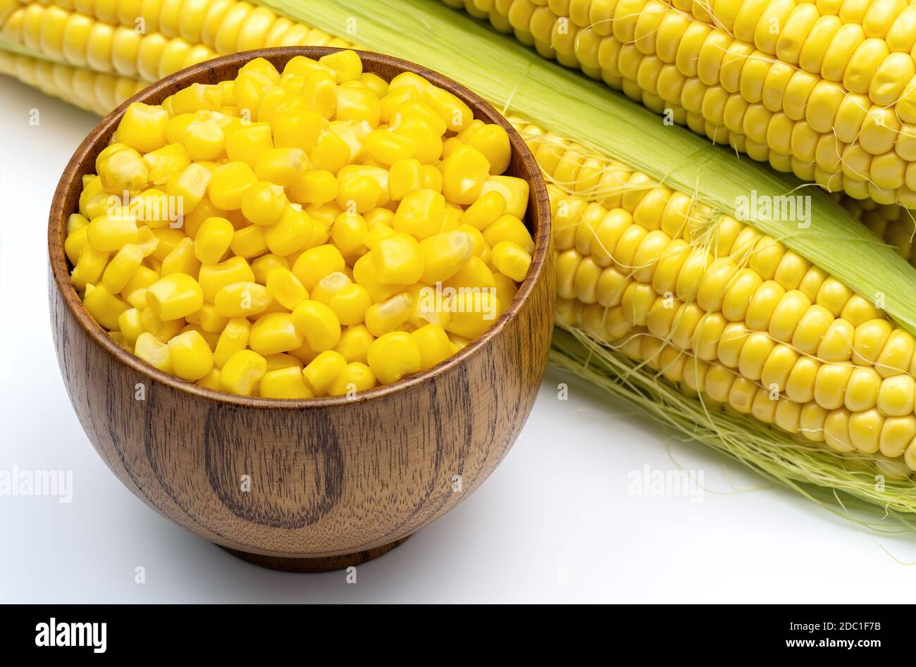 Sweet corn grains in wooden bowl on the background of fresh corn cobs ...