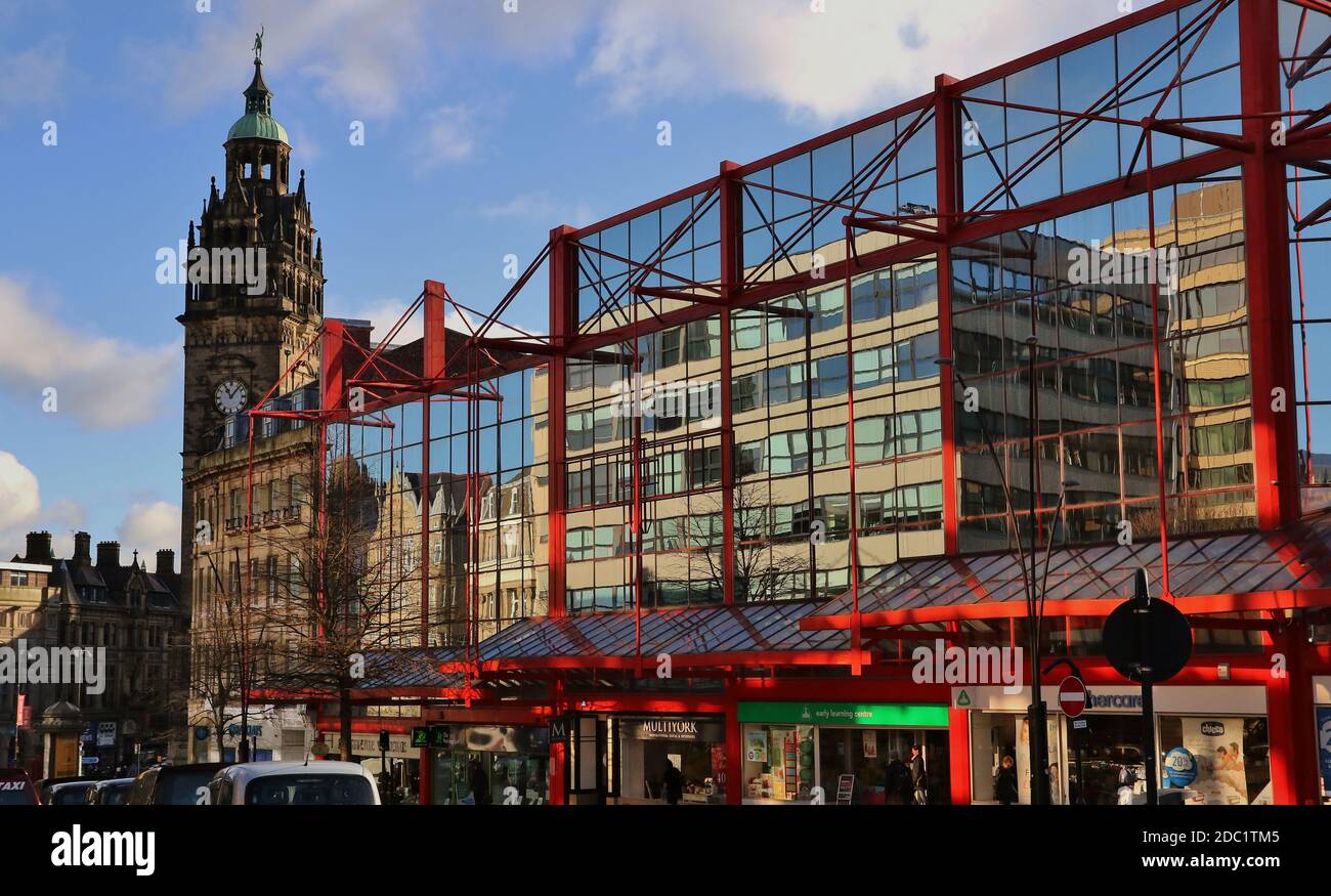 Tower of Sheffield Town Hall beyond reflections of modern office block in windows of the shops ...