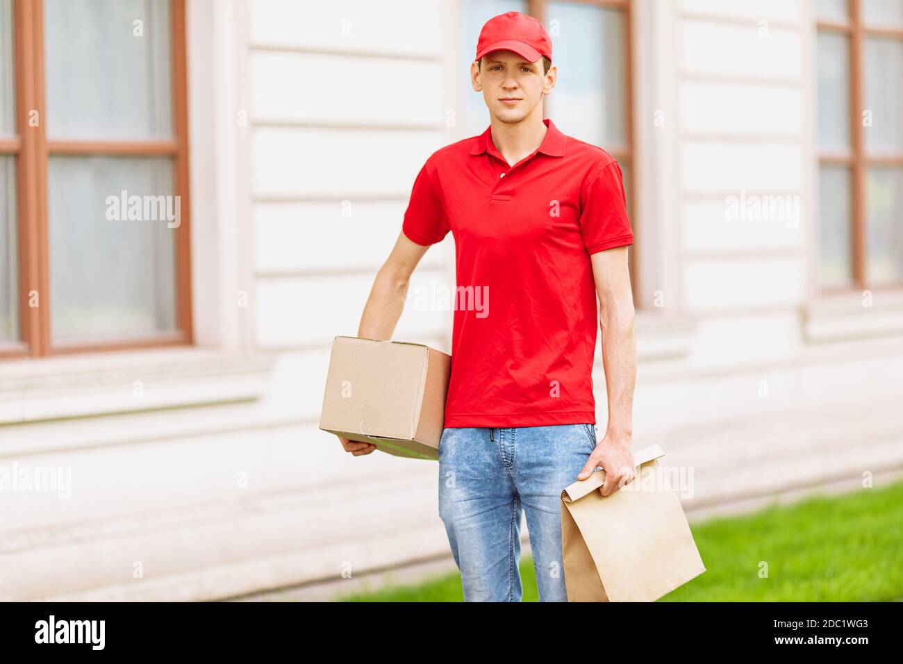 A uniformed courier with a cardboard box in his hands and a paper bag ...