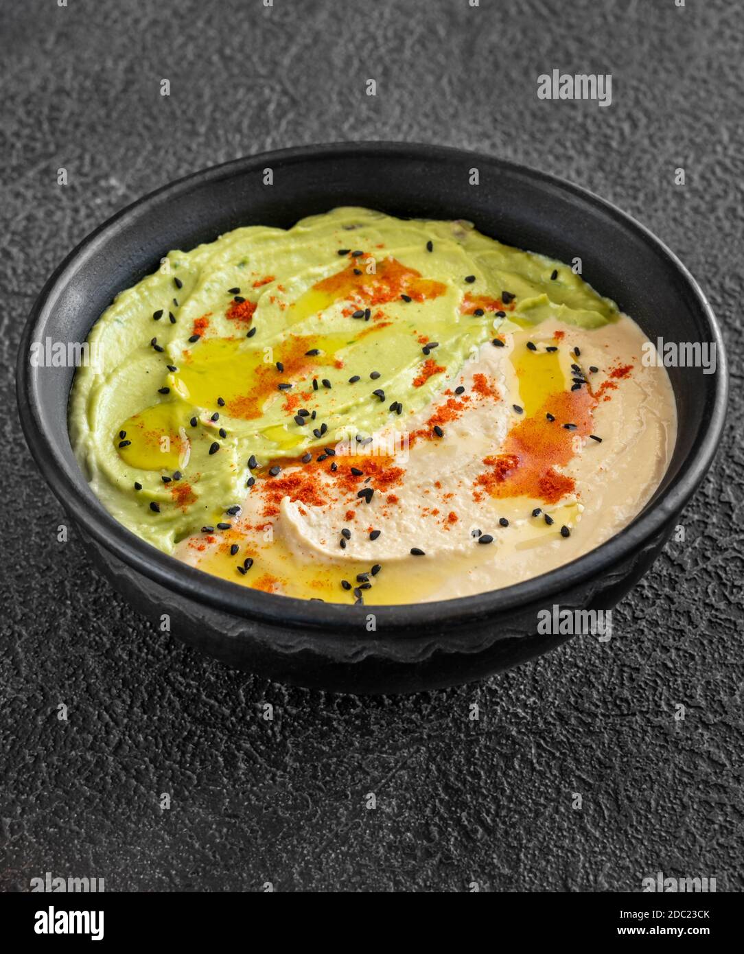 Bowl of guacamole and hummus mix on black background Stock Photo - Alamy