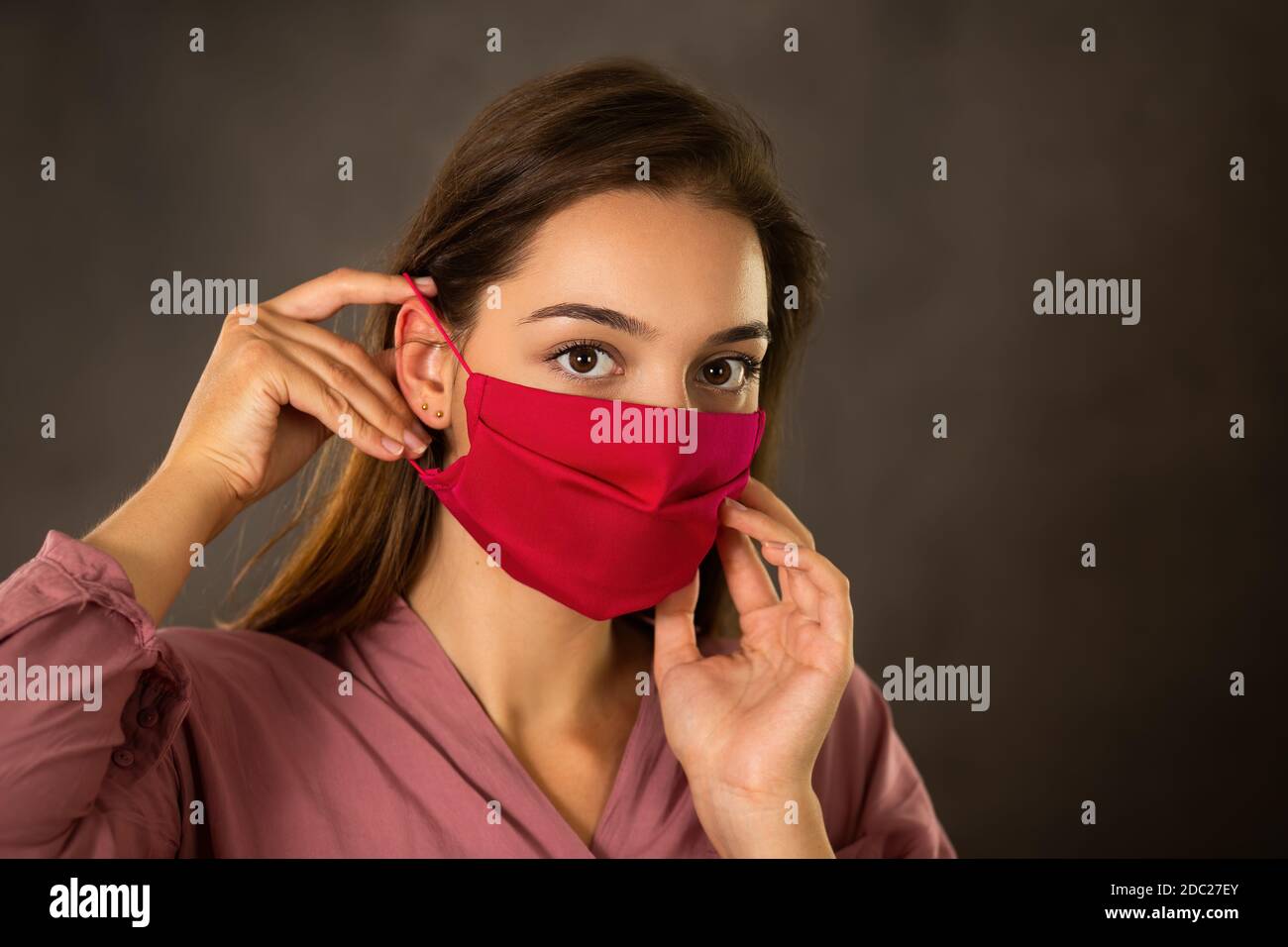 Woman attaching red cloth face mask on ear with fingers with dark ...