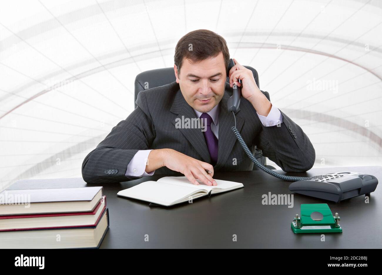 young executive at work and talking on phone at his desk at the office ...
