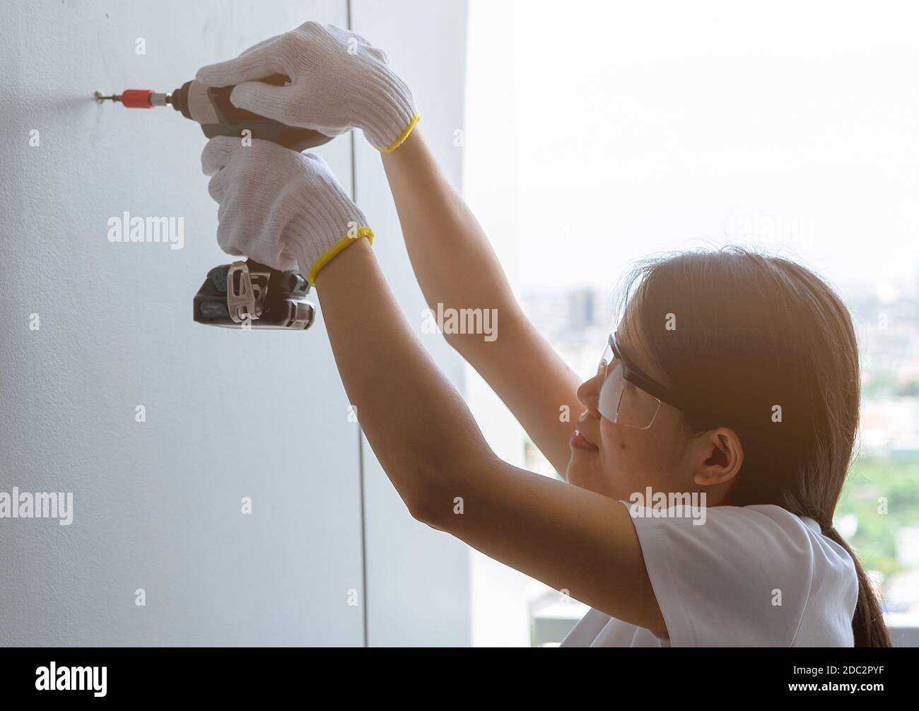 Asian woman drilling screw into apartment wall with cordless drill ...