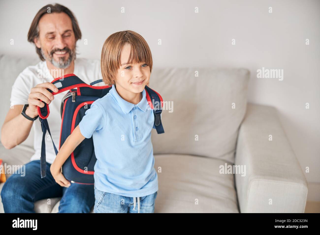Caring father assisting his child with putting backpack on Stock Photo ...