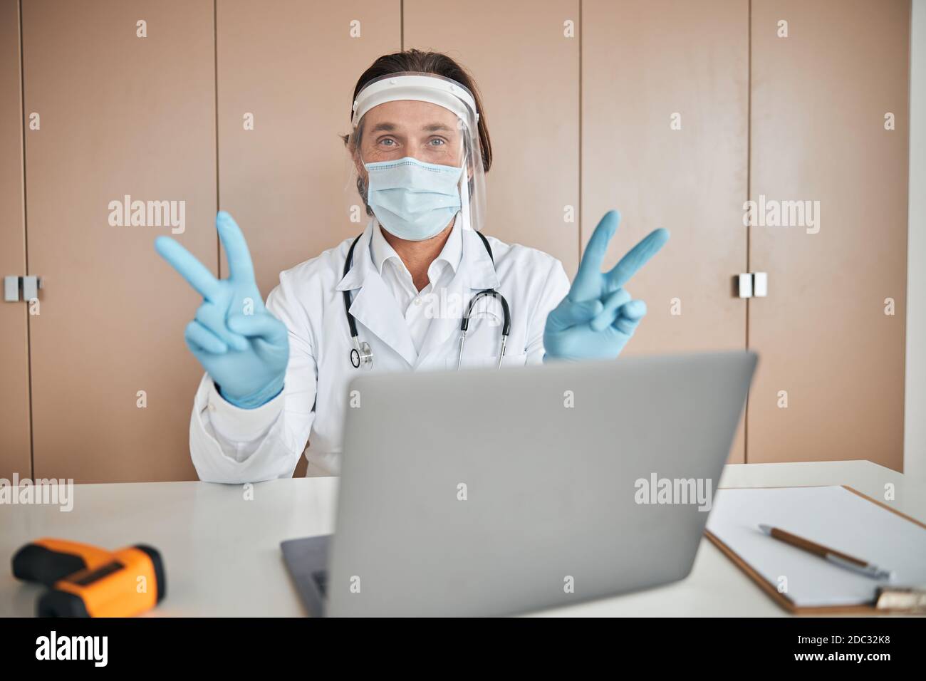 Optimistic doctor in mask showing victory signs with his hands Stock ...