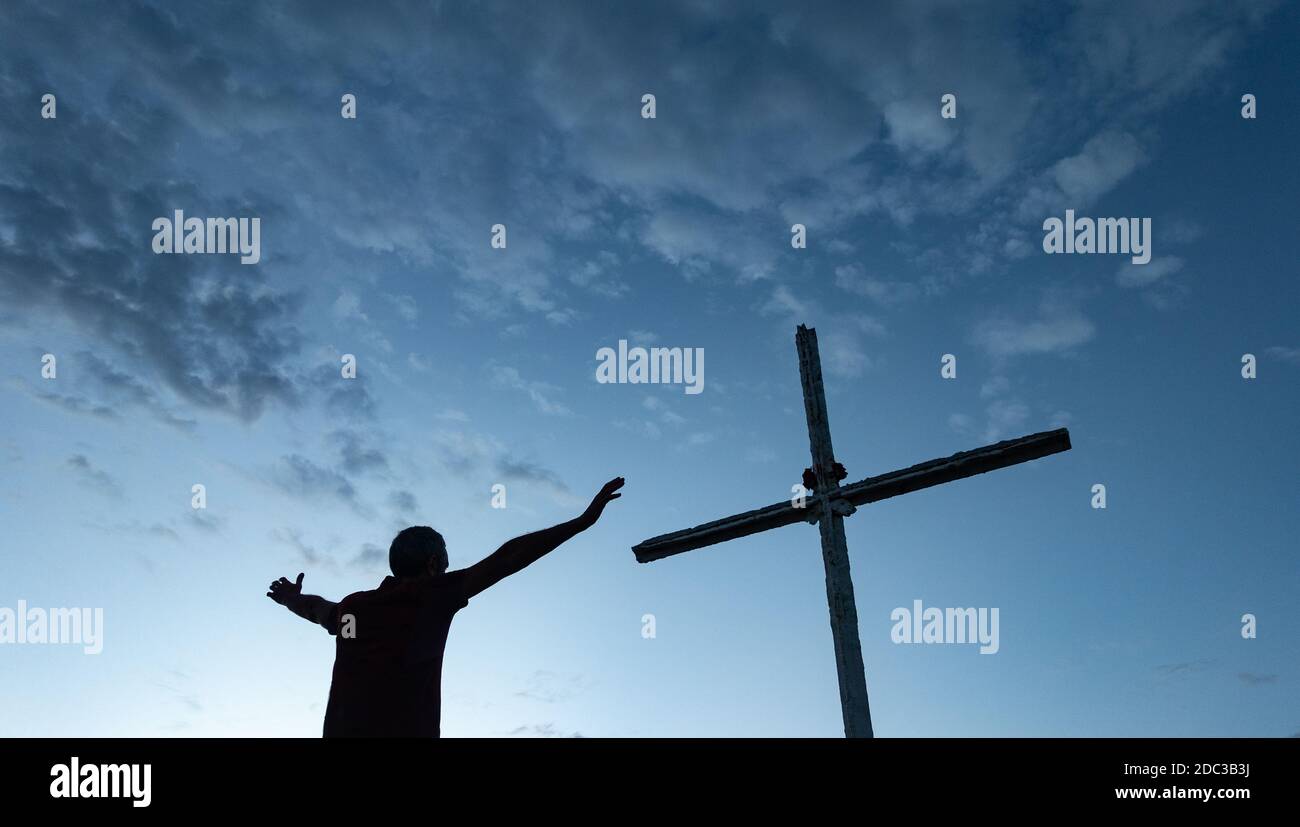 Man with arms outstretched praying under cross on mountain top Stock ...