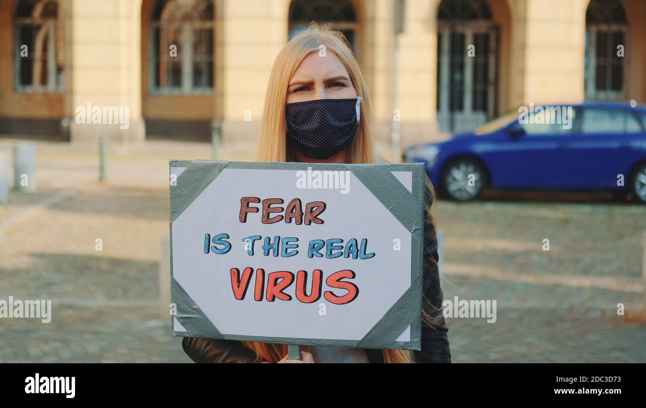 Blonde woman in protective mask protesting that fear is the real virus ...