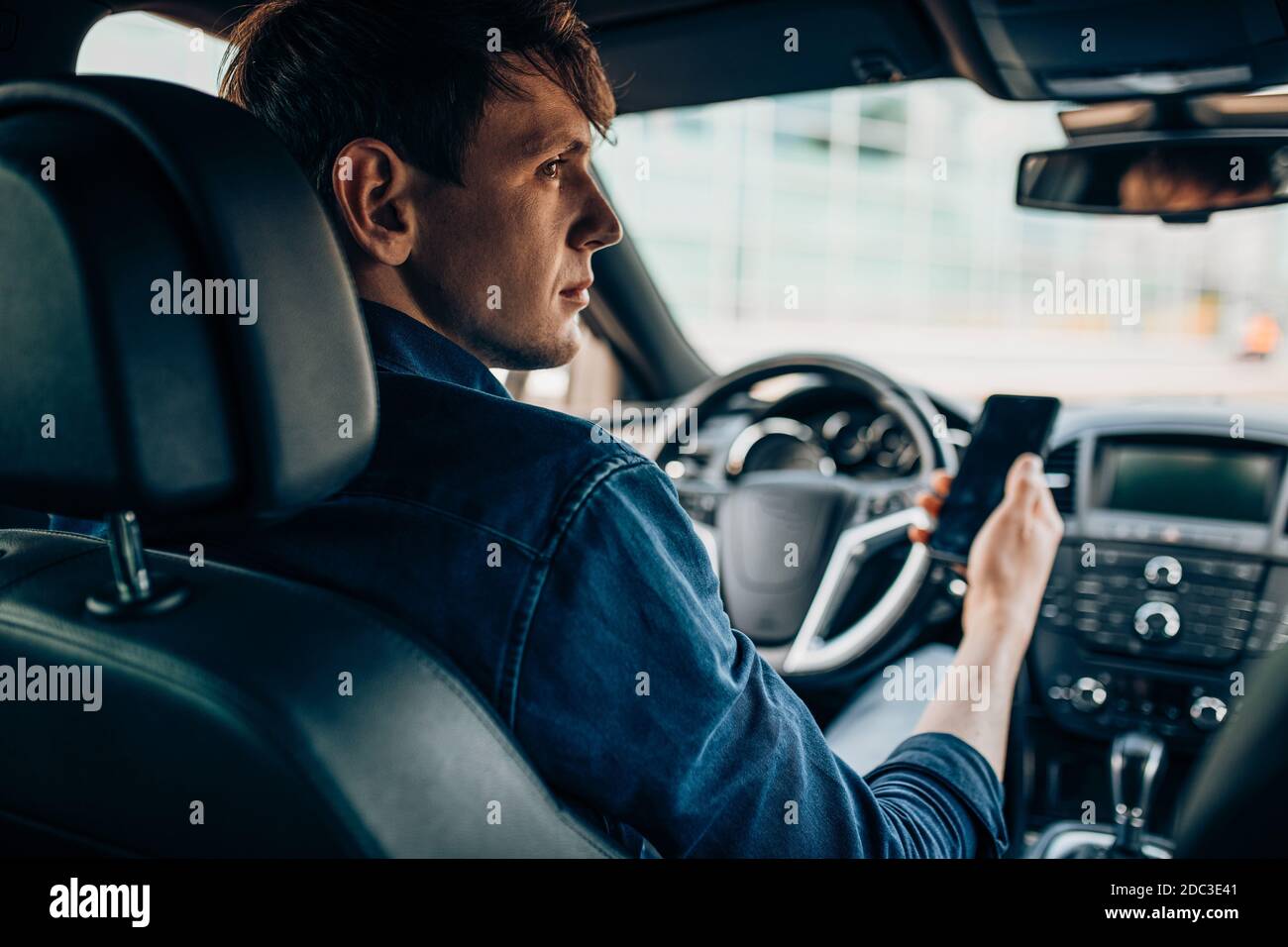 The man sitting behind the wheel of a car, using a mobile phone while ...