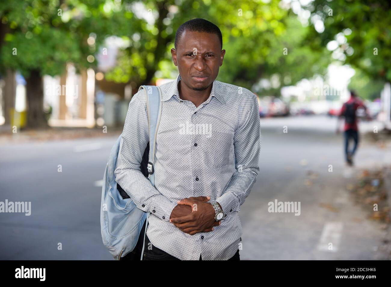 young man walking, carrying a backpack on the side and writhing pain ...