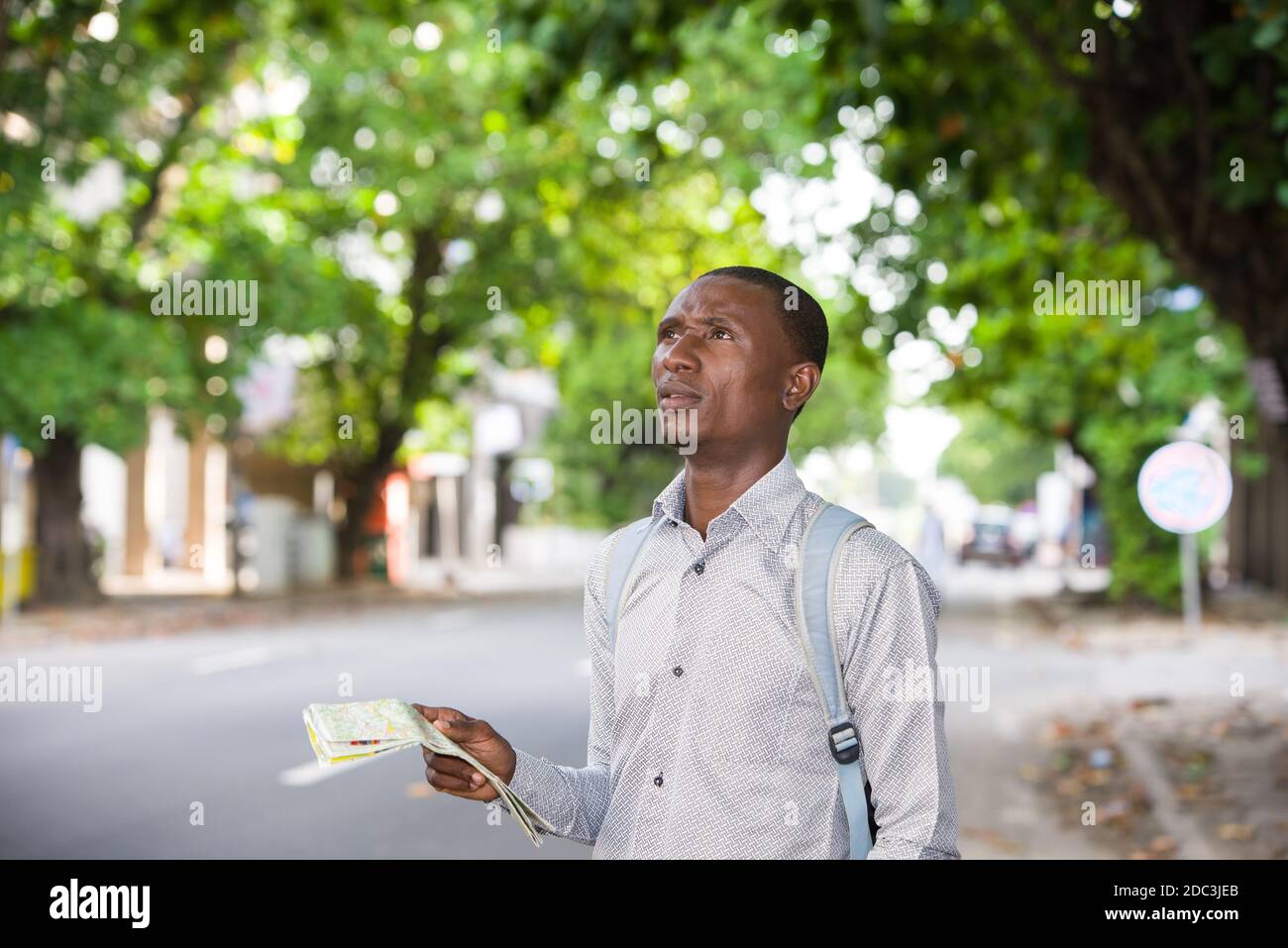 young man standing in shirt with map in hand thinking Stock Photo - Alamy