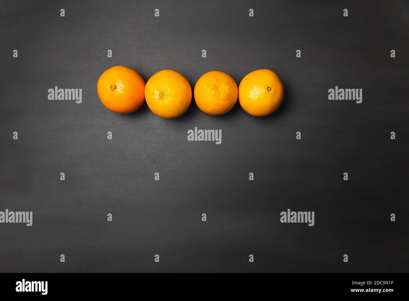 Four oranges arranged in line on black, dark background. Colorful fruit ...