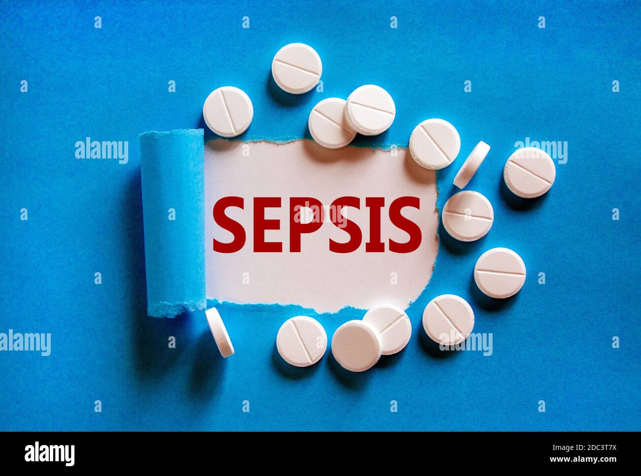 Word 'sepsis' appearing behind torn blue paper, white pills. Medical ...