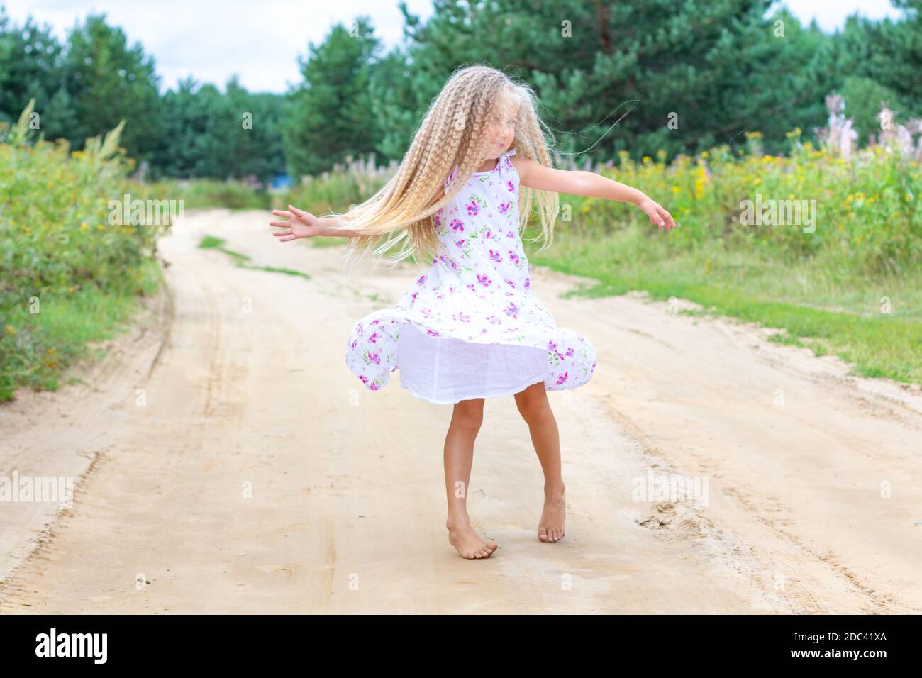 A girl with long blond curly hair is dancing, spinning on a forest road ...