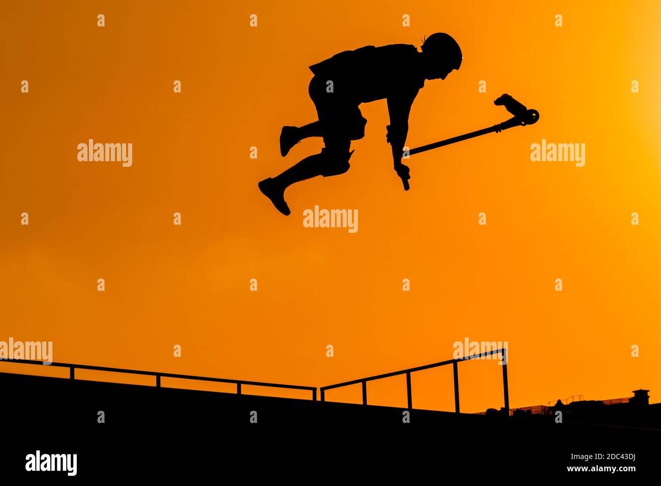 Teenager silhouette showing high jump tricks on scooter against sunset ...