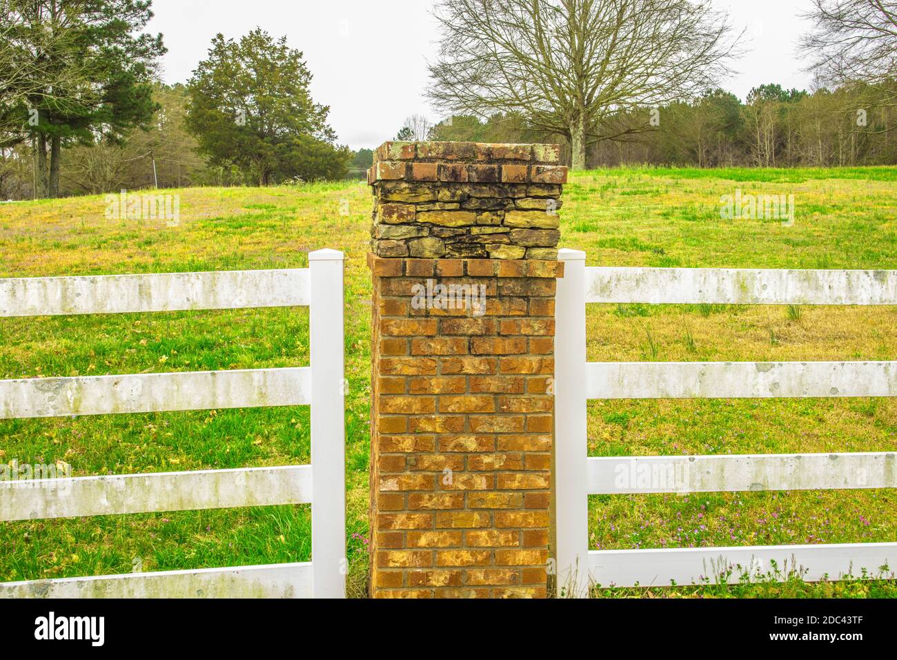 A brick fence post and a white wooden fence with beautiful green ...