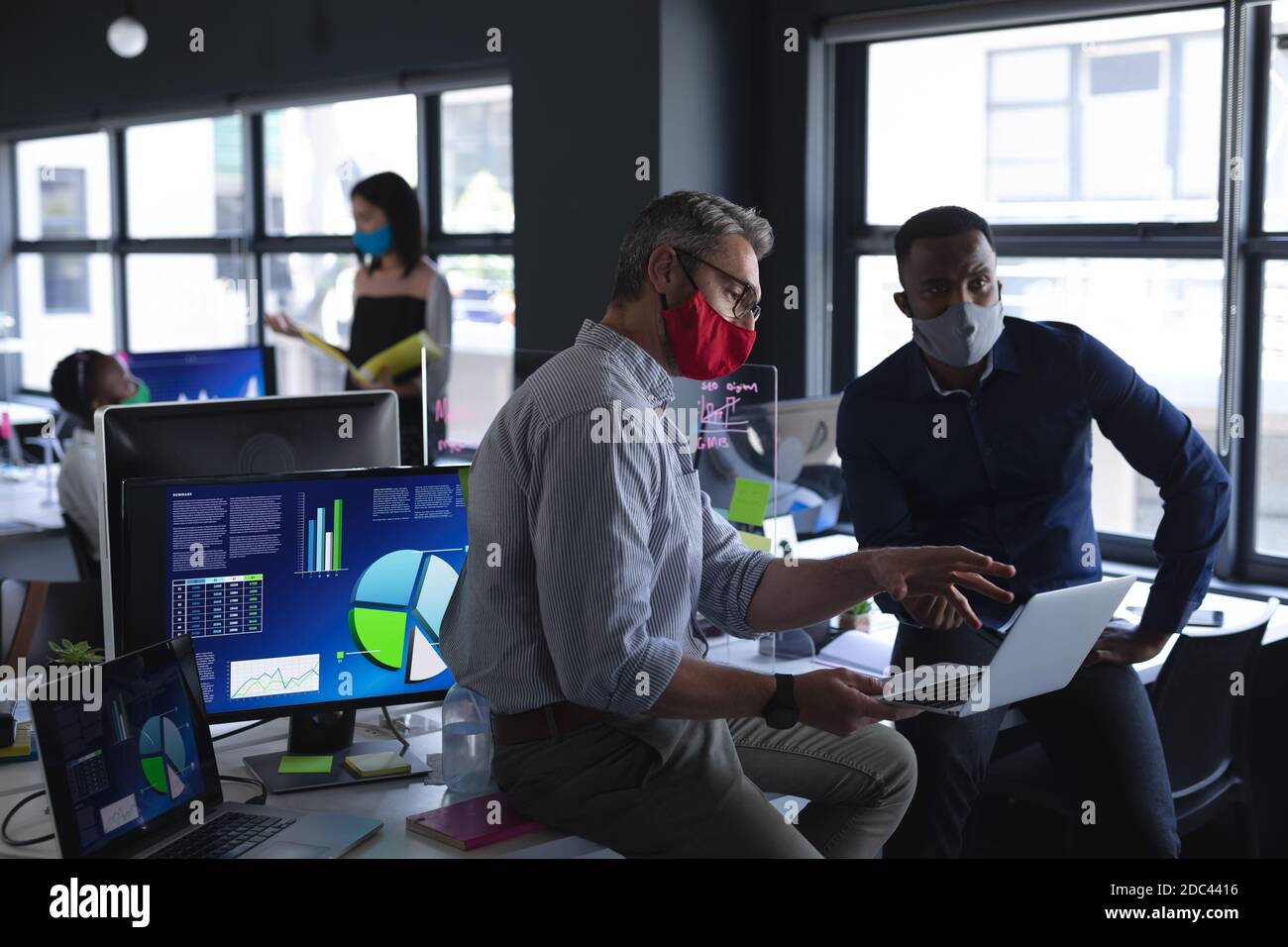 Diverse male colleagues using laptop while sitting over their desk at modern office Stock Photo ...