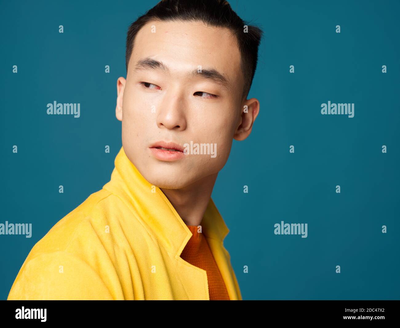 Portrait of Asian man in yellow t-shirt on blue background cropped view ...