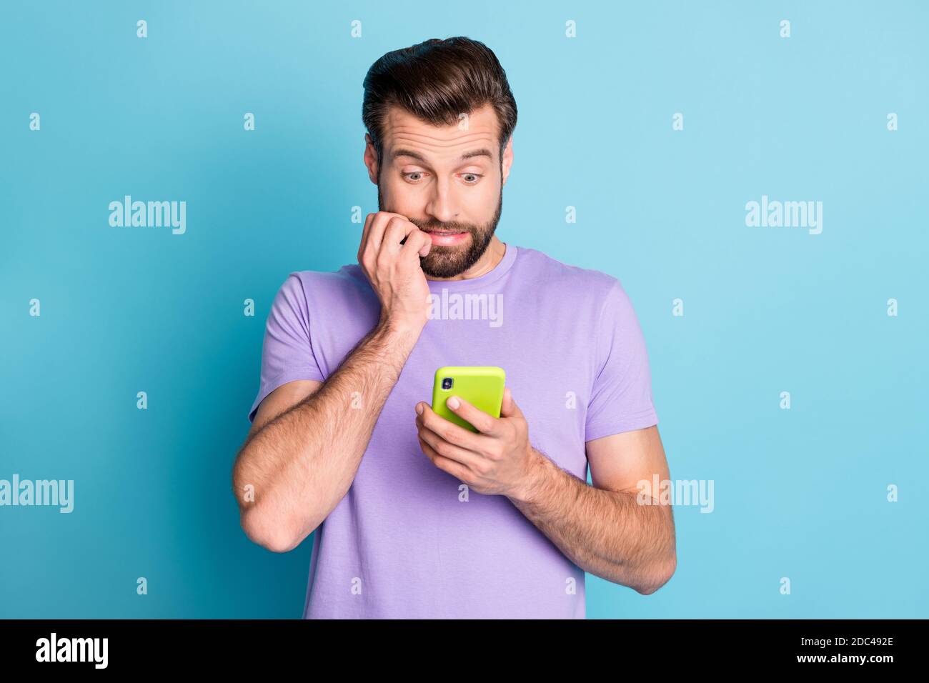 Photo portrait of astonished man keeping smartphone biting fingers ...