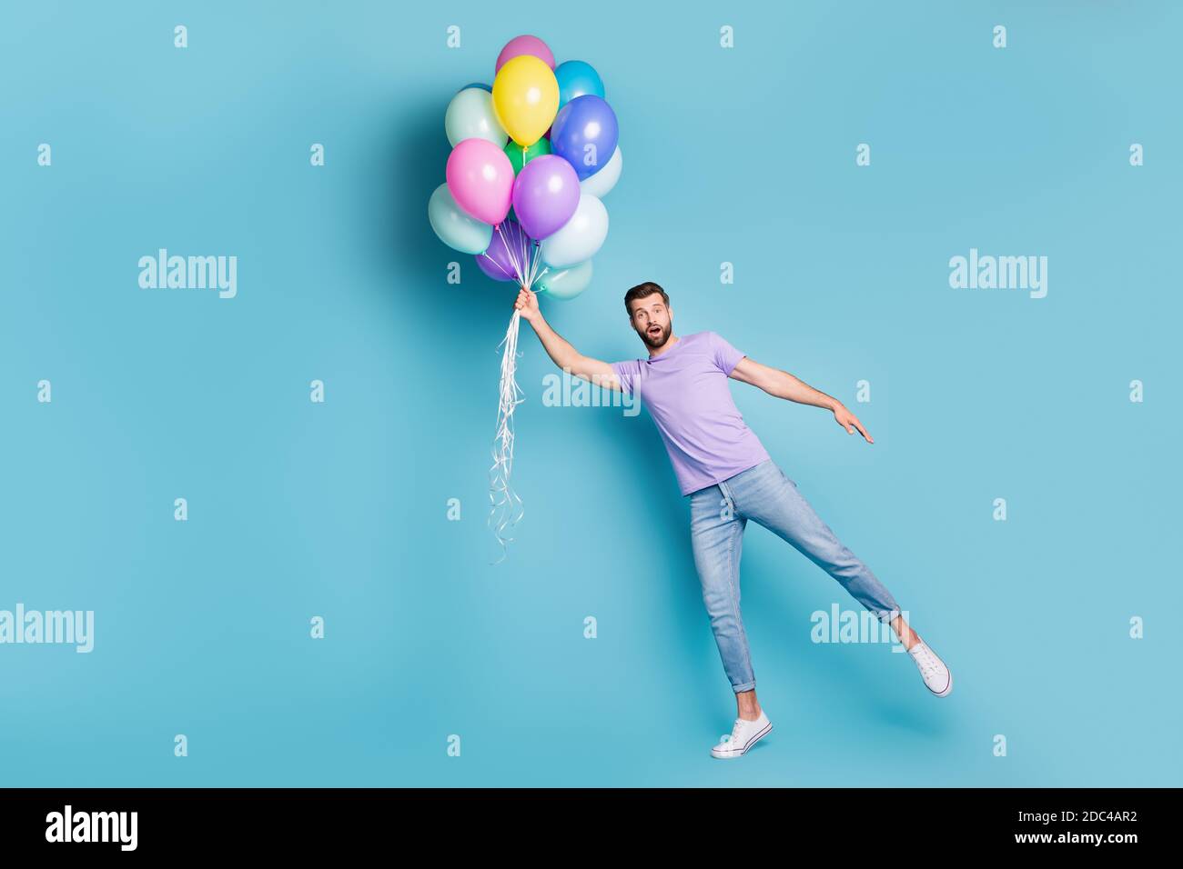 Photo portrait of shocked man holding helium ballons in one hand ...