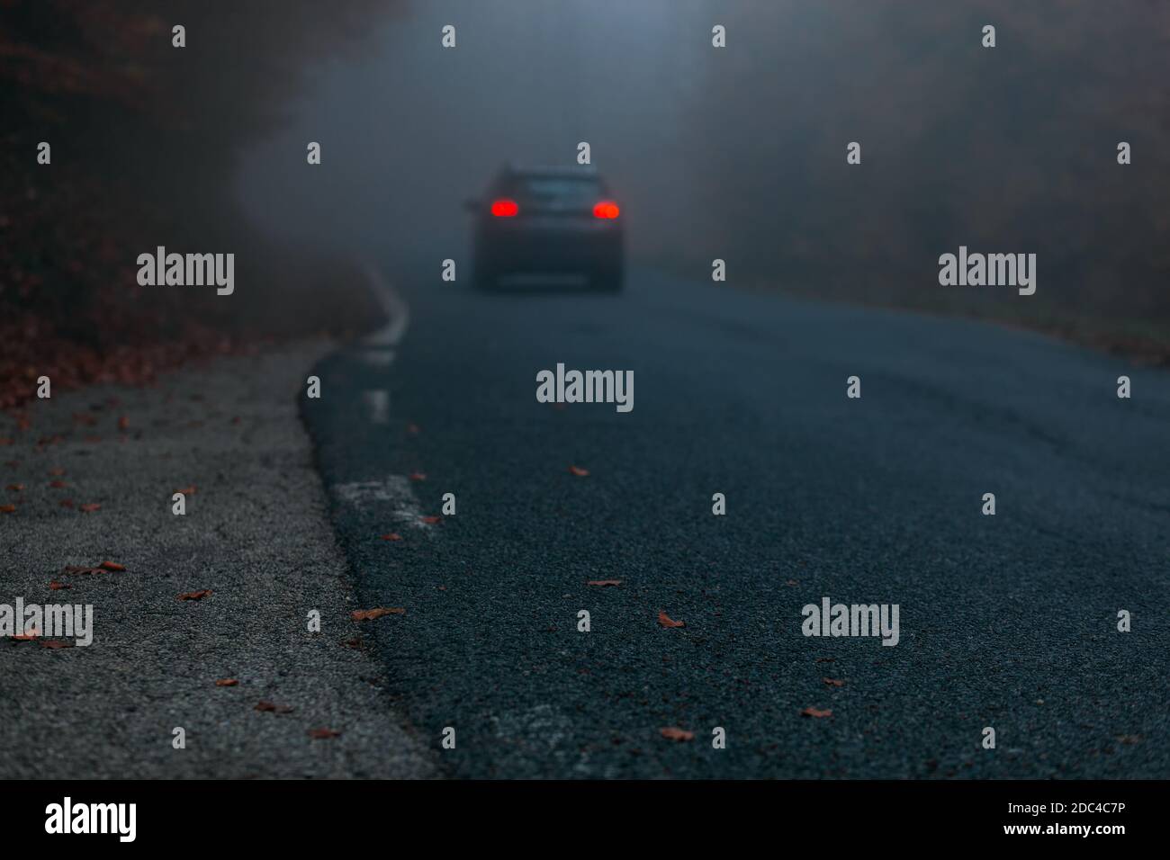 Lonely car on the mountain road covered in thick fog with red lights on ...